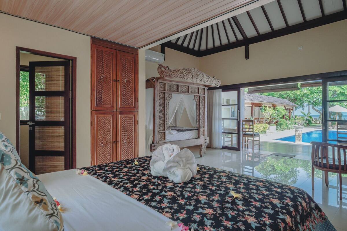 Quarto com cama, guarda-roupa de madeira e vista para uma piscina ao ar livre.