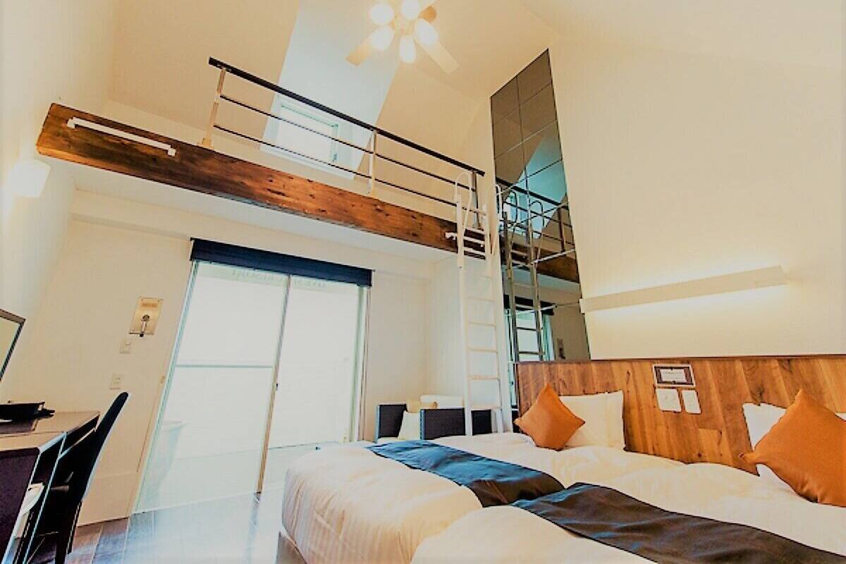 Quarto com beliche, escrivaninha, cadeira, escada e uma janela grande.