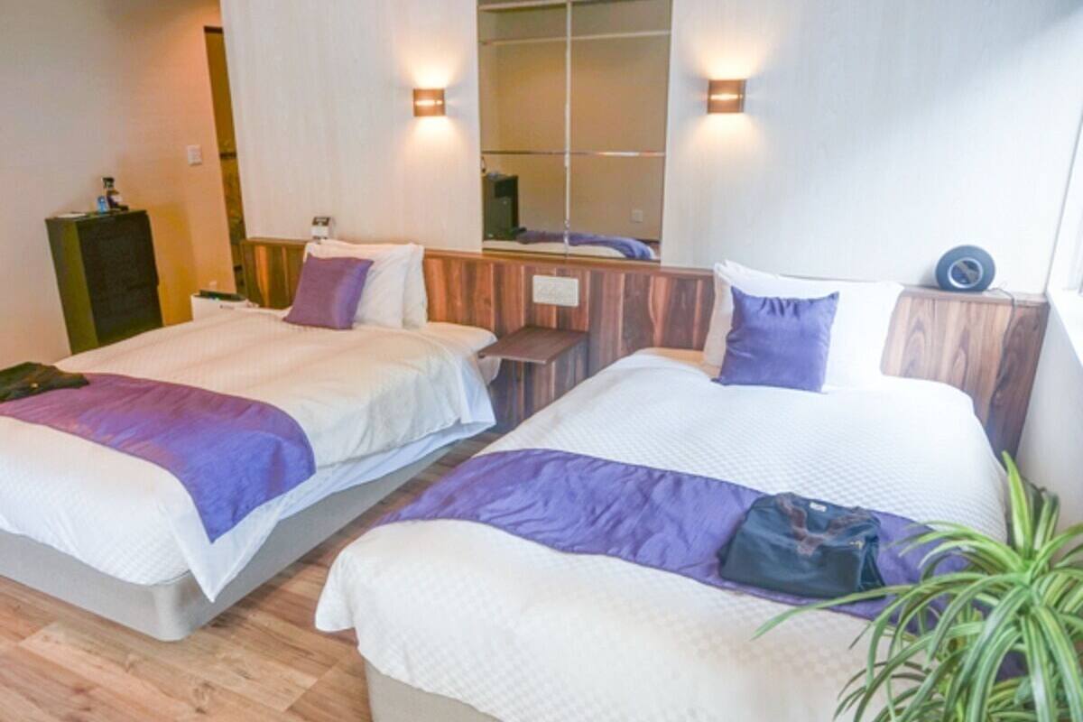 Quarto de hotel com duas camas, uma escrivaninha pequena e um espelho.