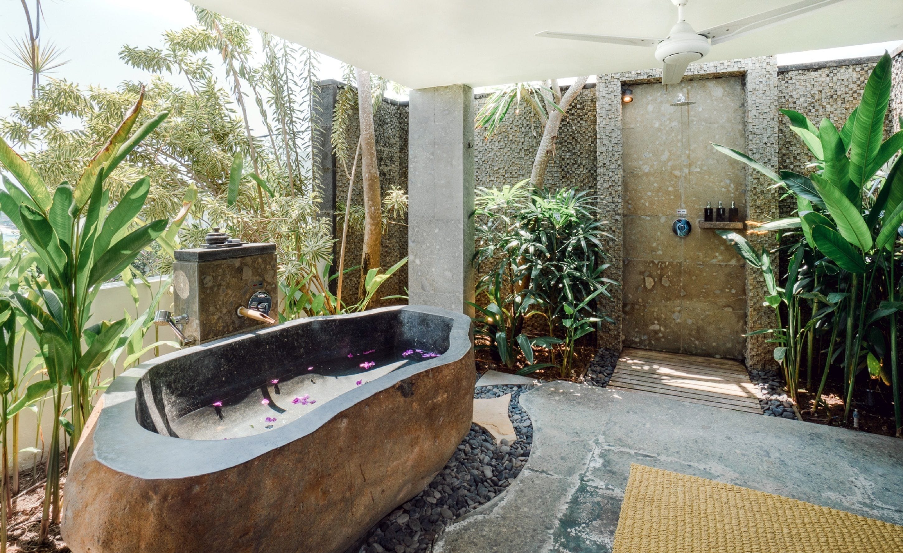 Uma área de spa com uma banheira independente, um ventilador de teto e uma parede de pedra.