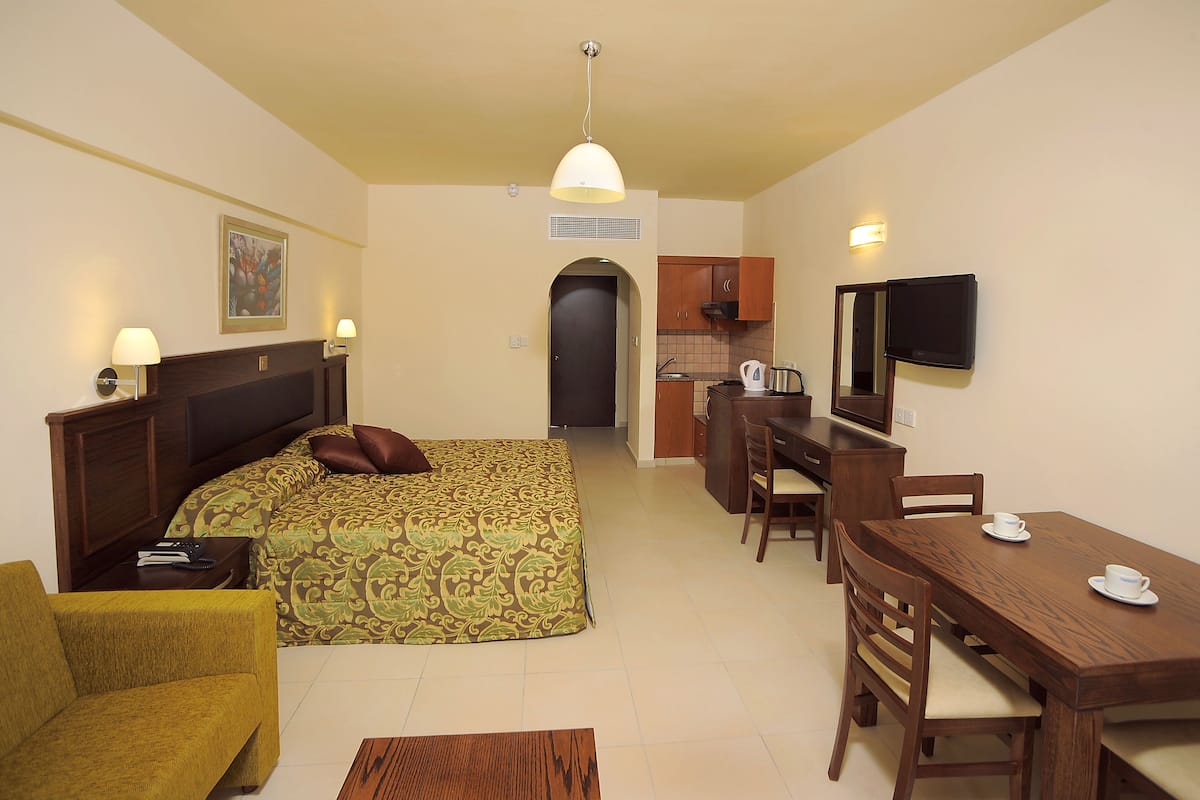 Quarto de hotel com cama, escrivaninha, cadeira, televisão e cozinha.