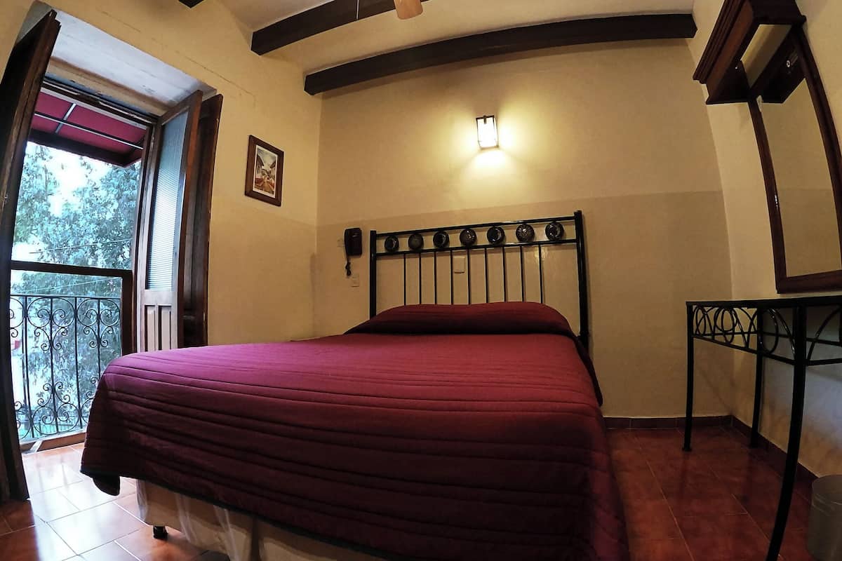 Quarto com cama, luminária na parede, janela com vista e uma mesinha.
