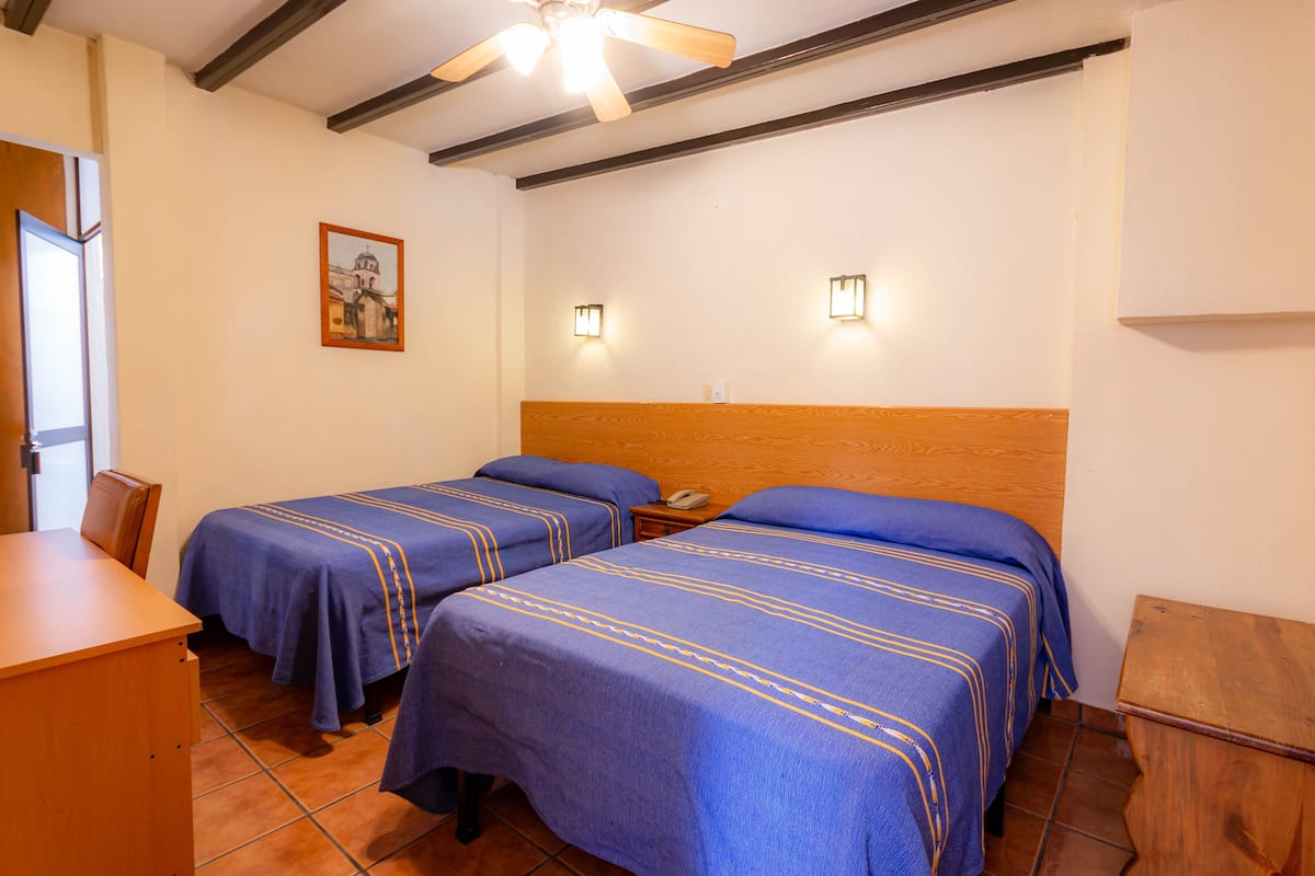 Quarto de hotel com duas camas, cabeceira de madeira, uma escrivaninha e uma cadeira.