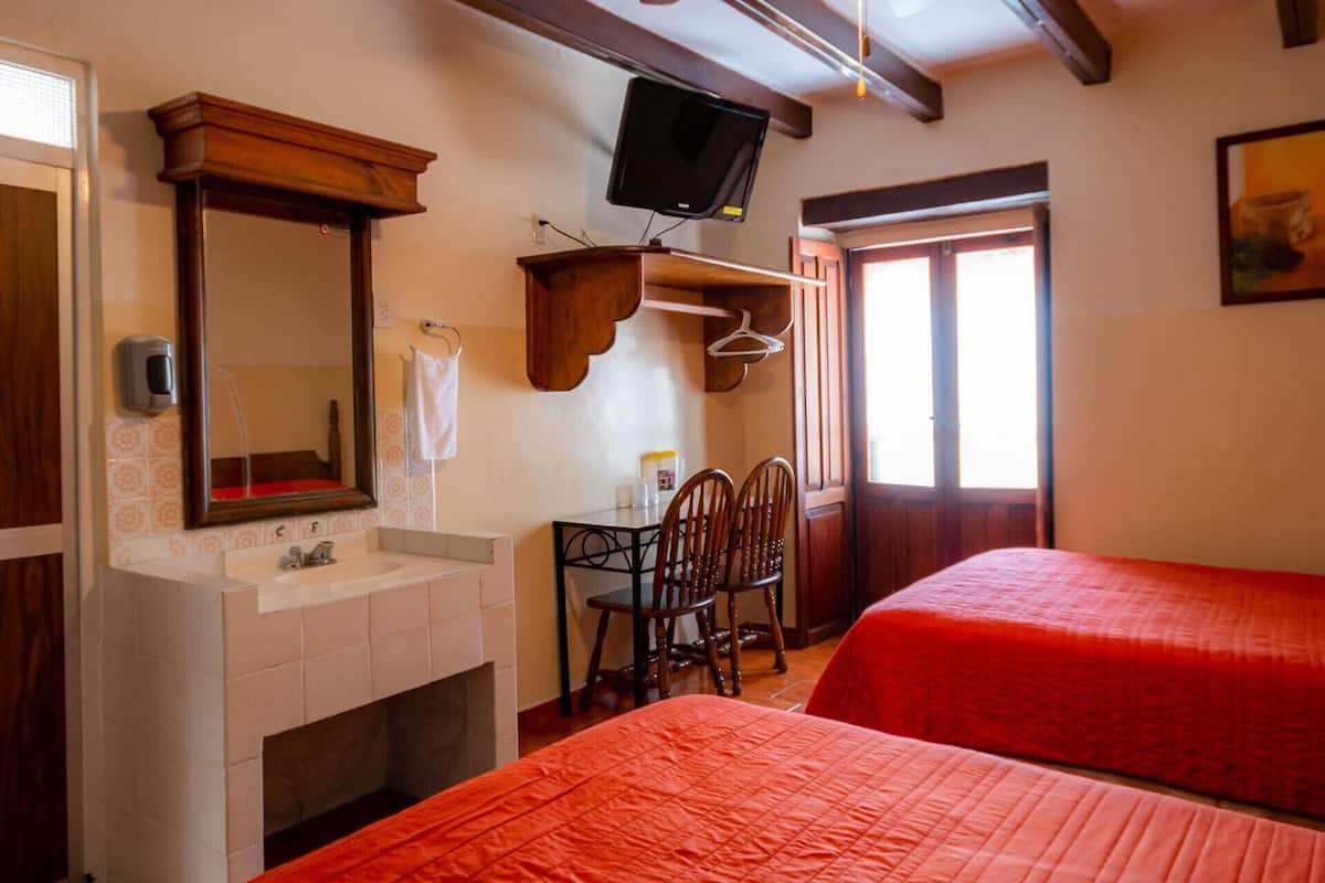 Quarto com duas camas, um ventilador de teto, pia e televisão.