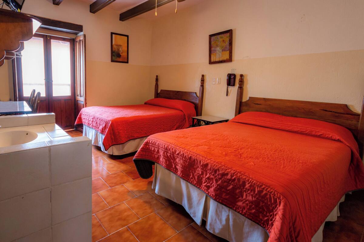 Quarto de hotel com duas camas, banheiro e janela com cortinas.