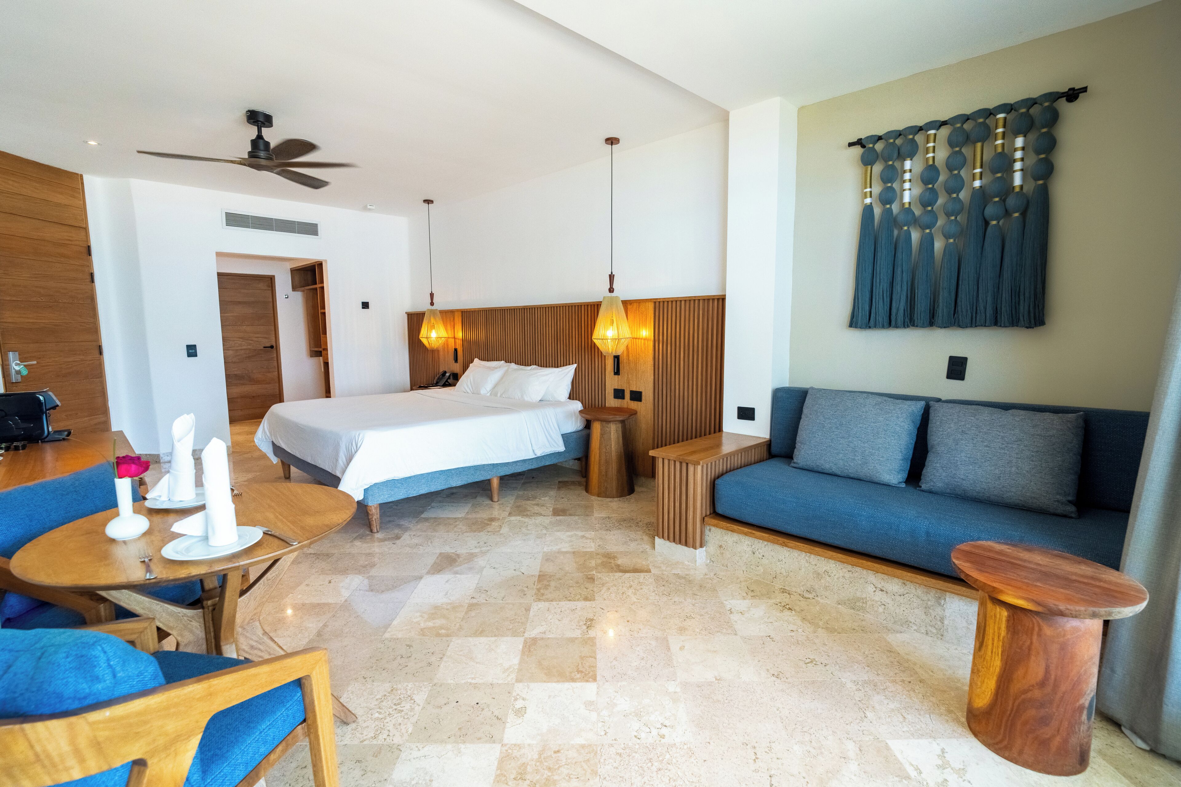 Quarto de hotel com cama, sofá, mesa de jantar e ventoinha no teto.
