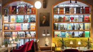 Uma livraria com várias estantes cheias de livros, um sofá e cadeiras vermelhas.