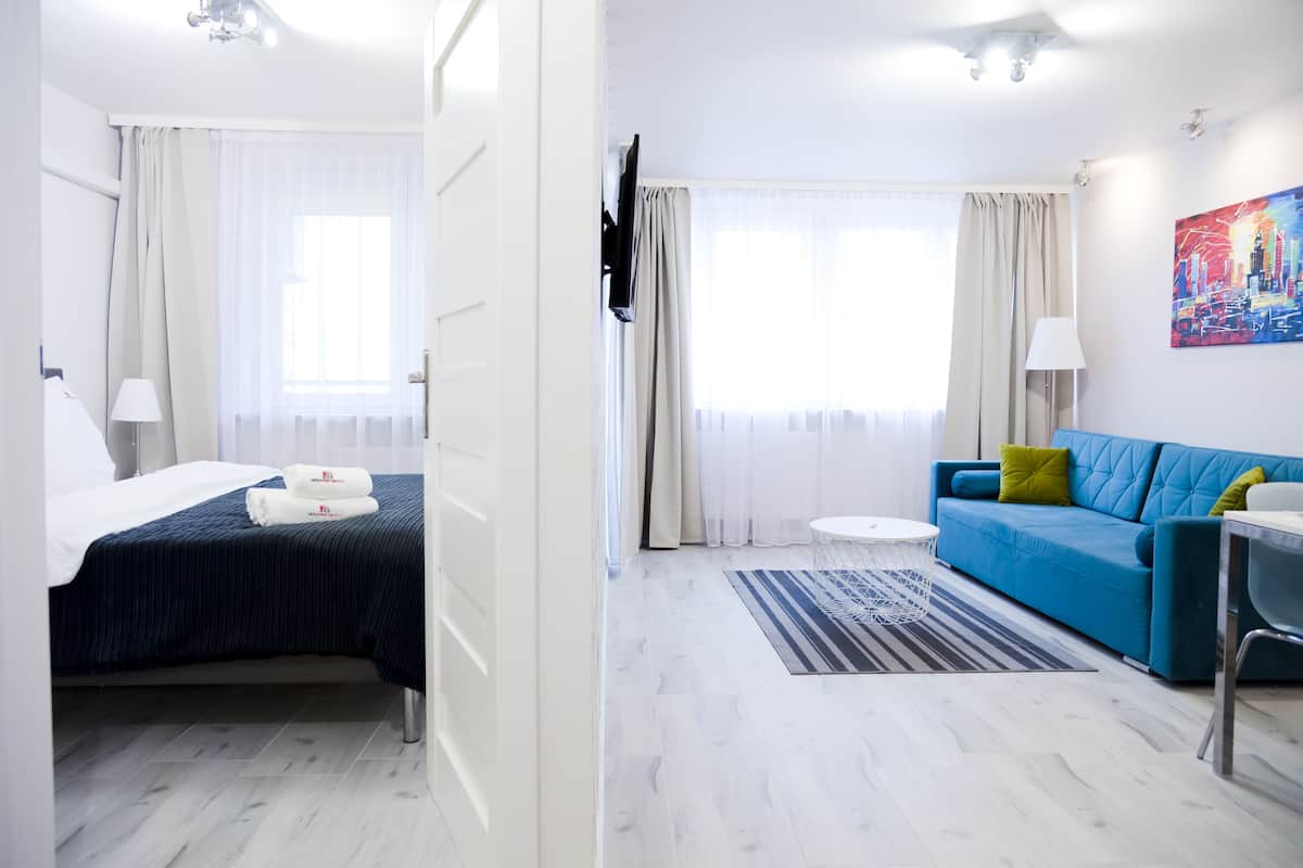 Quarto de hotel com cama, sofá azul, televisão e pintura na parede.