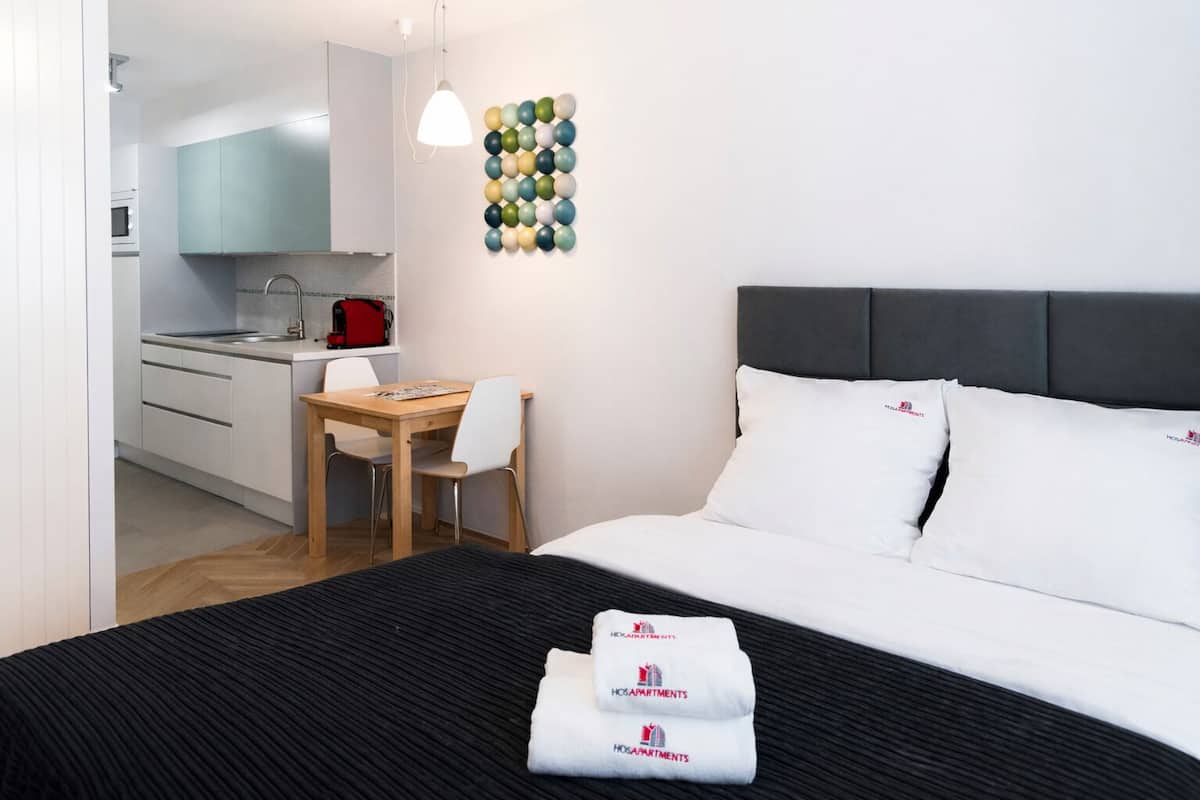 Quarto de hotel com cama, escrivaninha, cadeira, área de cozinha e um ornamento na parede.