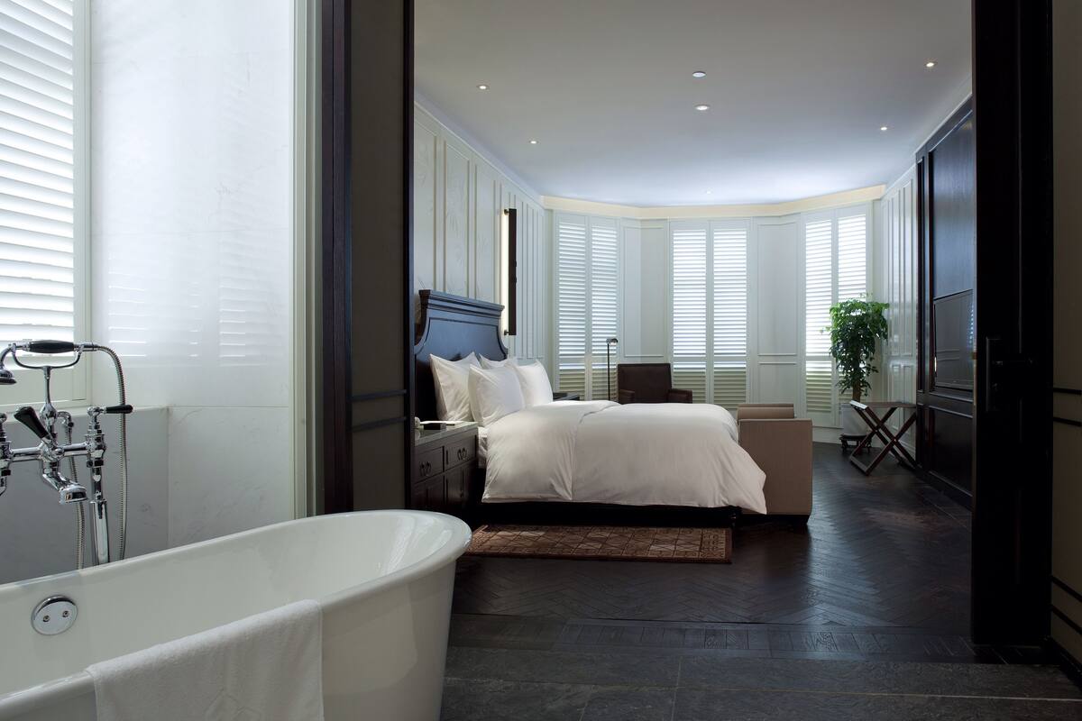 Quarto moderno com uma cama grande, uma banheira e vista para o exterior através de amplas janelas.