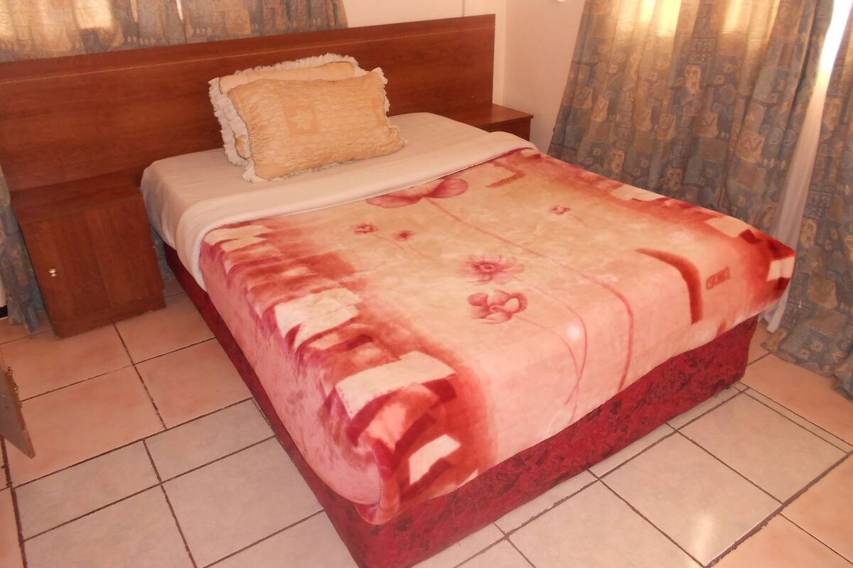 Uma cama com cabeceira de madeira, colcha florida e um travesseiro.