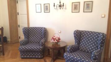 Quarto com duas poltronas estampadas, uma pequena mesa redonda com um vaso de flores e um candelabro fixado na parede.