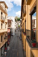 Uma rua estreita ladeada por edifícios altos, com varandas adornadas com plantas em vasos e um céu azul claro.