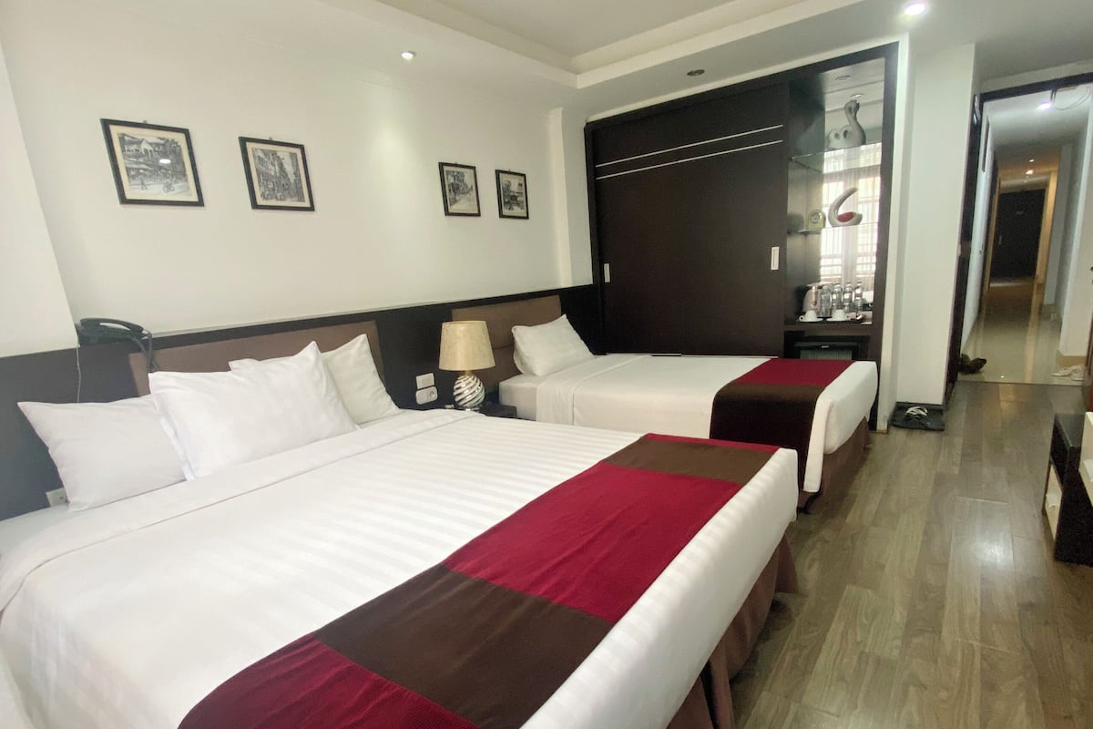 Quarto de hotel com duas camas, mesa de cabeceira, abajur e armário.