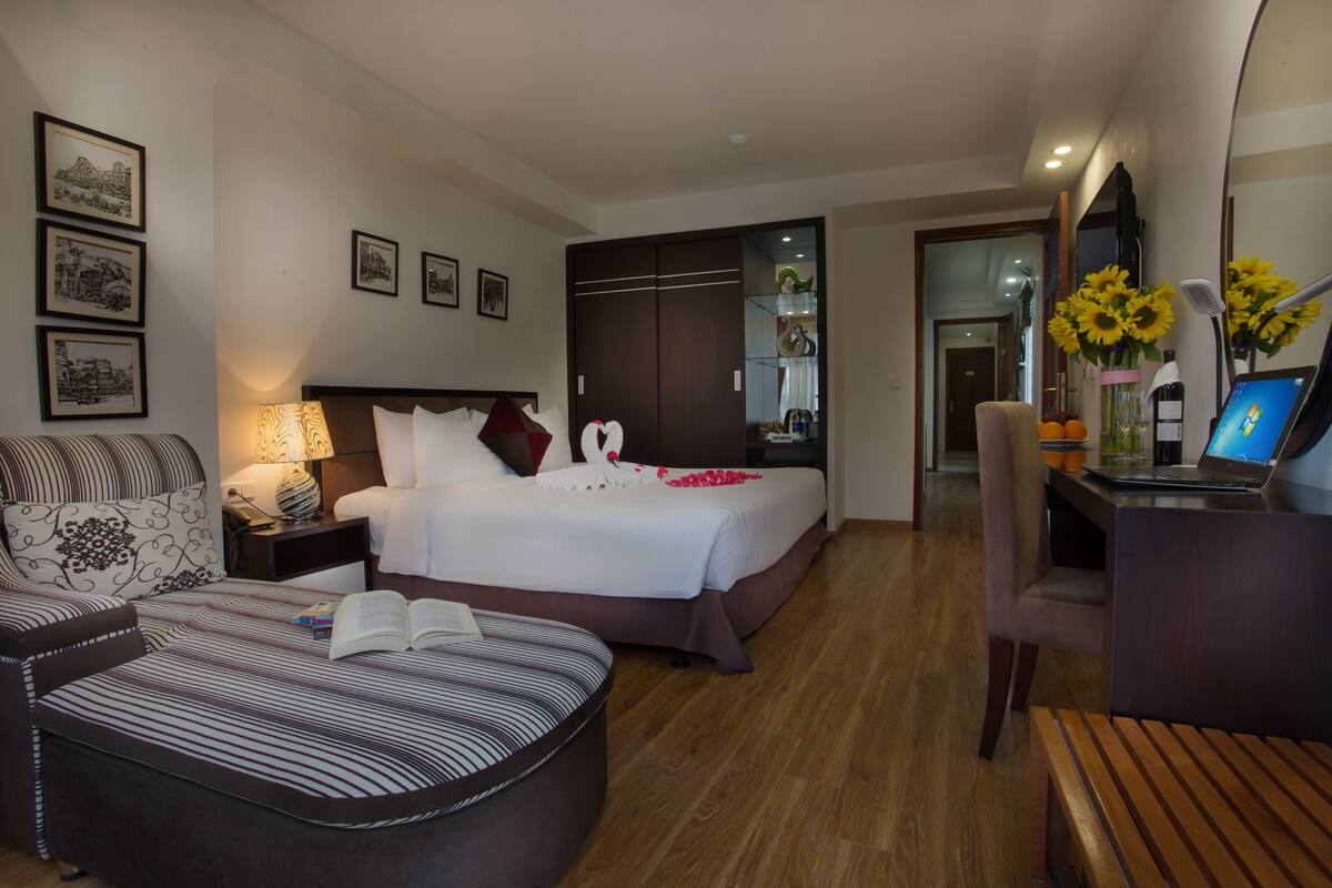 Quarto de hotel com cama, escrivaninha, poltrona, sofá e mesa de cabeceira com abajur.