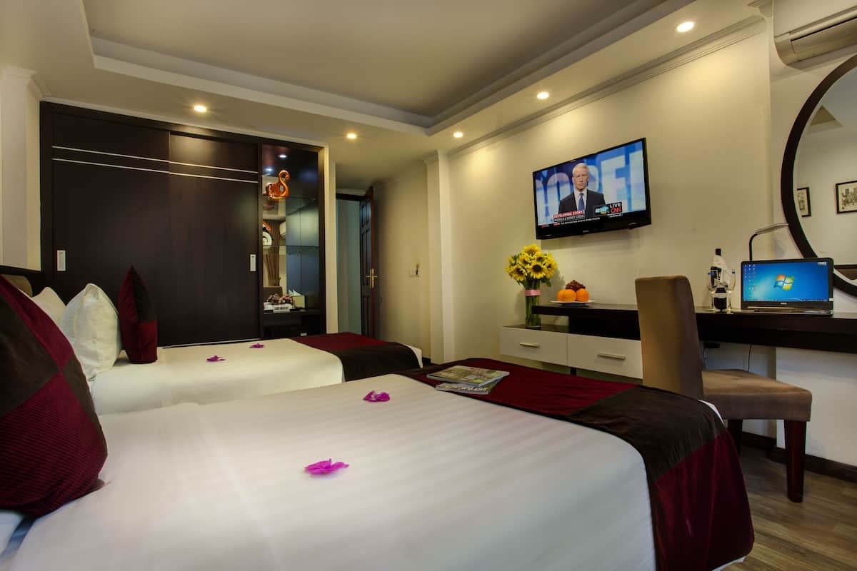 Quarto de hotel com duas camas, uma escrivaninha com computador, televisão e espelho.