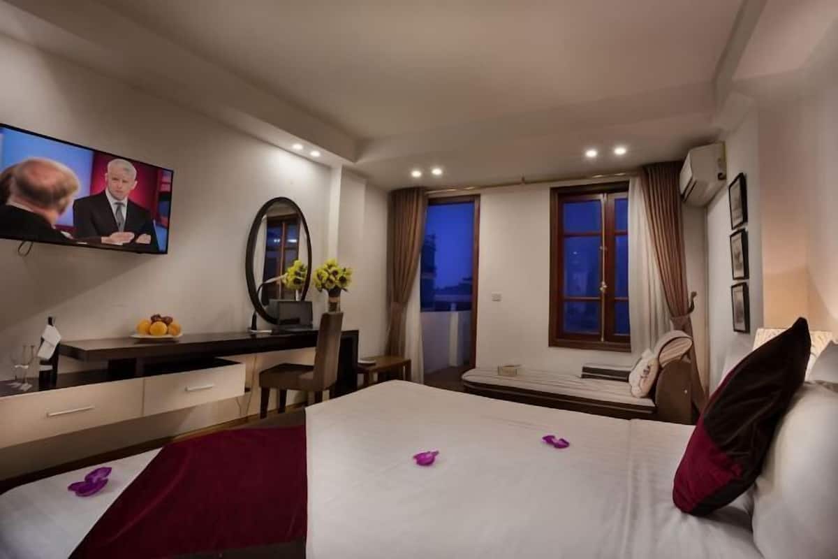 Quarto de hotel com uma cama, escrivaninha, televisão, espelho, janela e porta que dá para uma varanda.