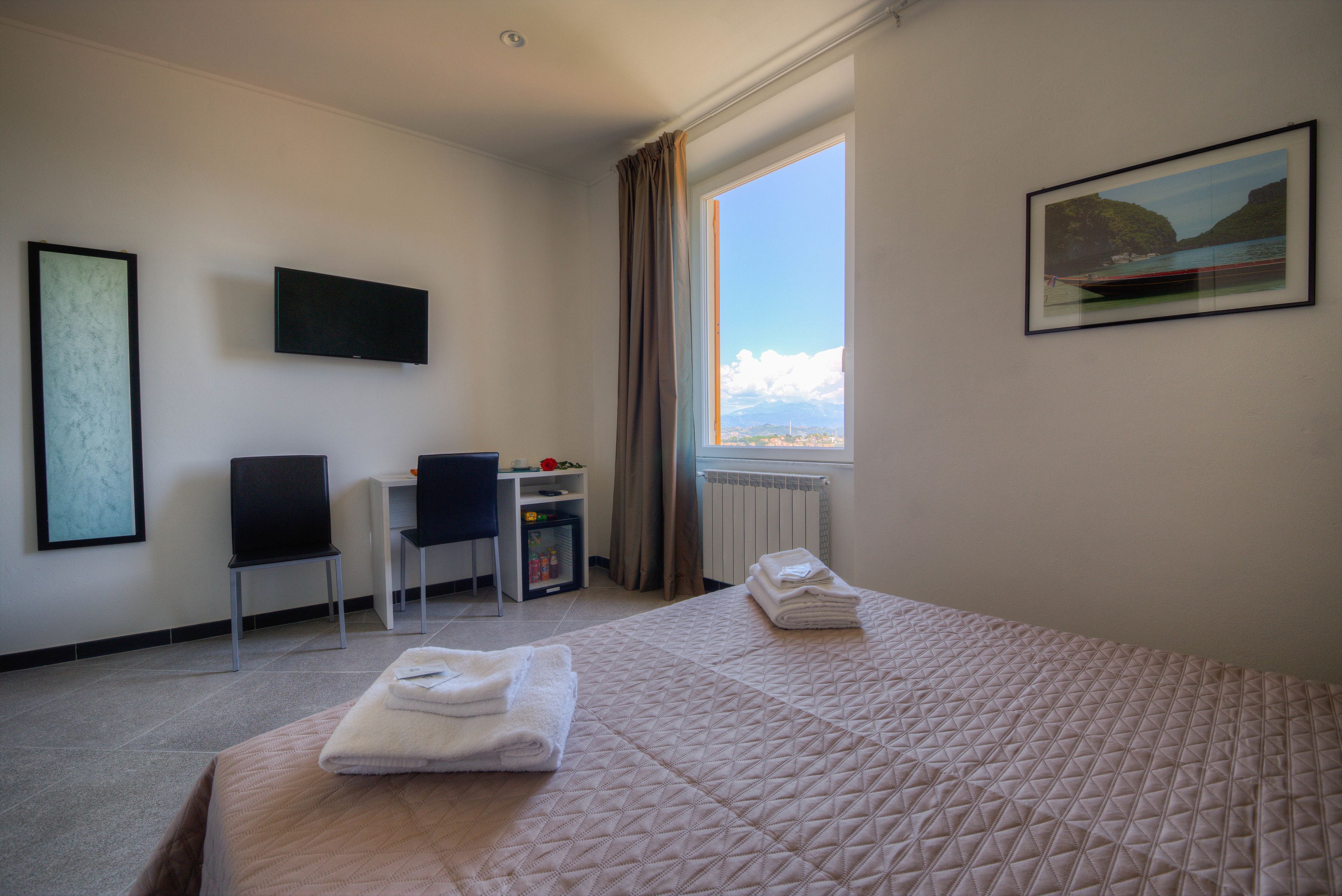 Quarto de hotel com cama, escrivaninha, cadeira, televisão e janela com vista.