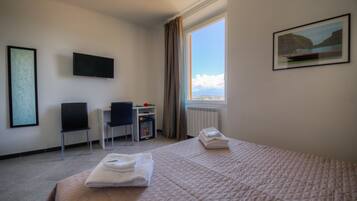 Quarto de hotel com cama, escrivaninha, cadeira, televisão e janela com vista.