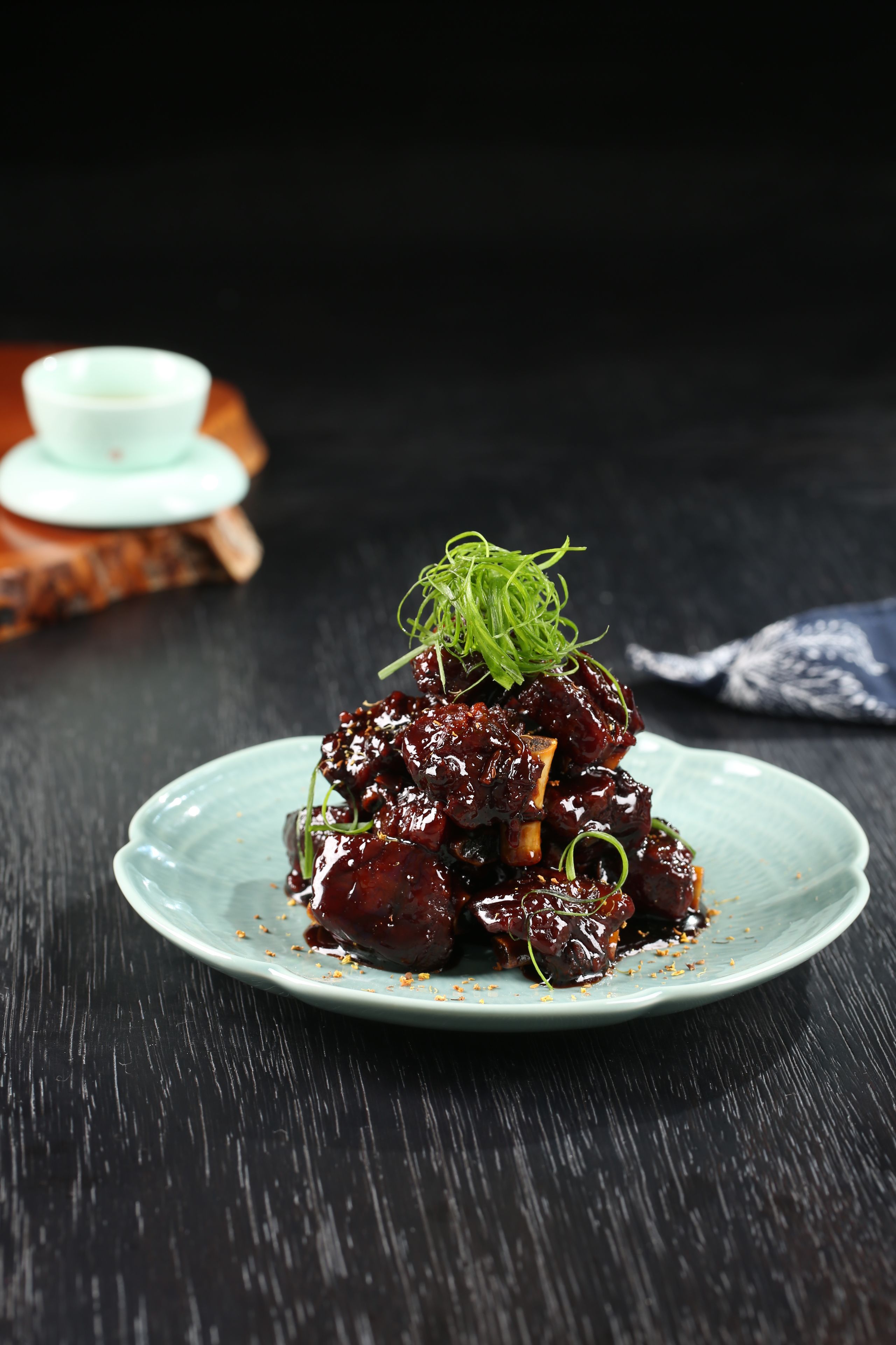 Prato de carne glaceada, guarnecida com ervas verdes, servido em um prato azul claro.
