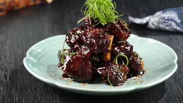 Prato de carne glaceada, guarnecida com ervas verdes, servido em um prato azul claro.