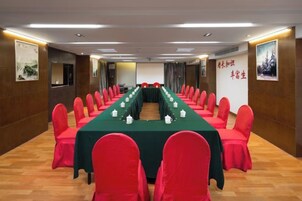 Uma sala de conferências com uma mesa comprida, cadeiras vermelhas e toalha de mesa verde.