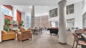 Um espaço interno amplo, com várias opções de assento, mesa de bilhar e janelas grandes que oferecem vista para um edifício de tijolos.