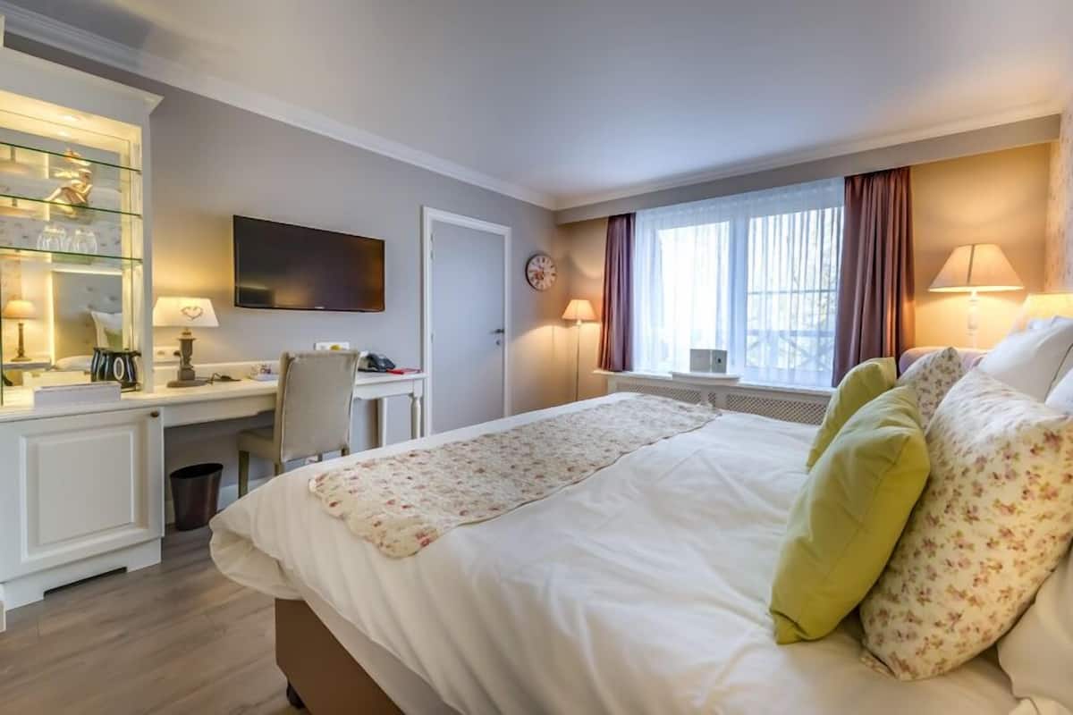 Quarto de hotel com cama, escrivaninha, cadeira e televisão.