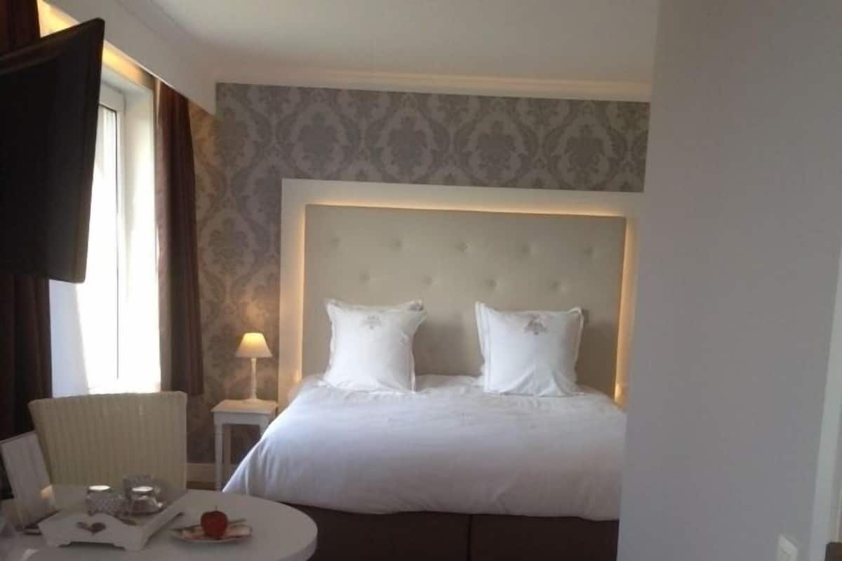 Quarto de hotel com uma cama, uma mesa redonda com abajur e uma cadeira.