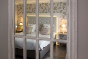 Quarto com uma cama grande, duas mesas de cabeceira com abajures, papel de parede floral e cabeceira estofada.
