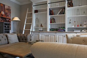 Sala de estar com sofá, mesa de centro e estante repleta de livros e objetos decorativos.