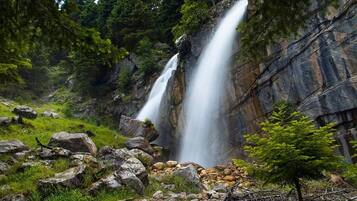 Uma cascata em área arborizada, com pedras e árvores.