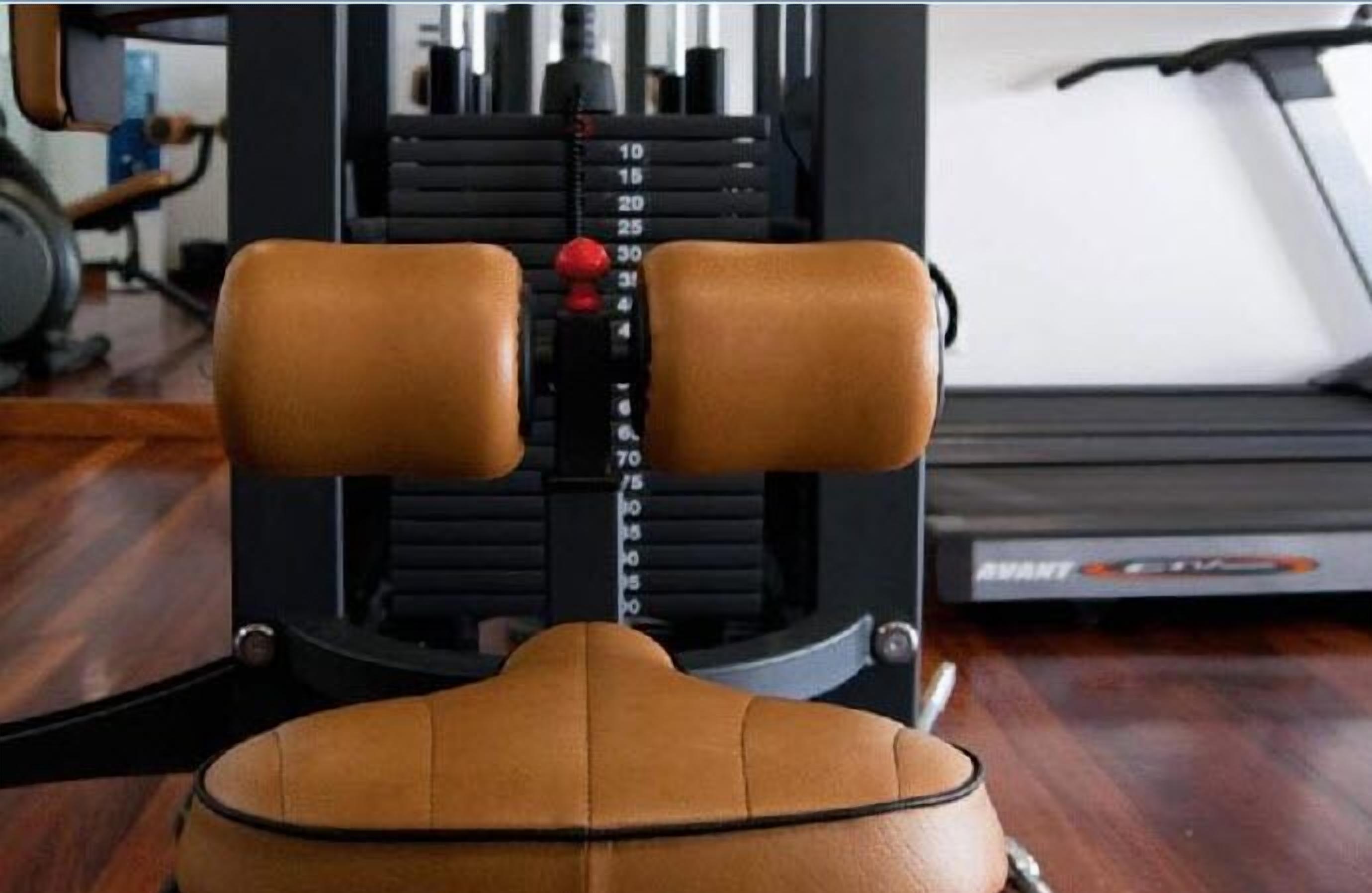 Uma academia com um banco de musculação e uma esteira ao fundo.
