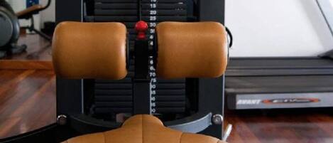Uma academia com um banco de musculação e uma esteira ao fundo.