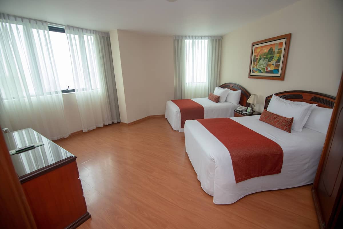 Quarto de hotel com duas camas, uma escrivaninha e um quadro na parede.