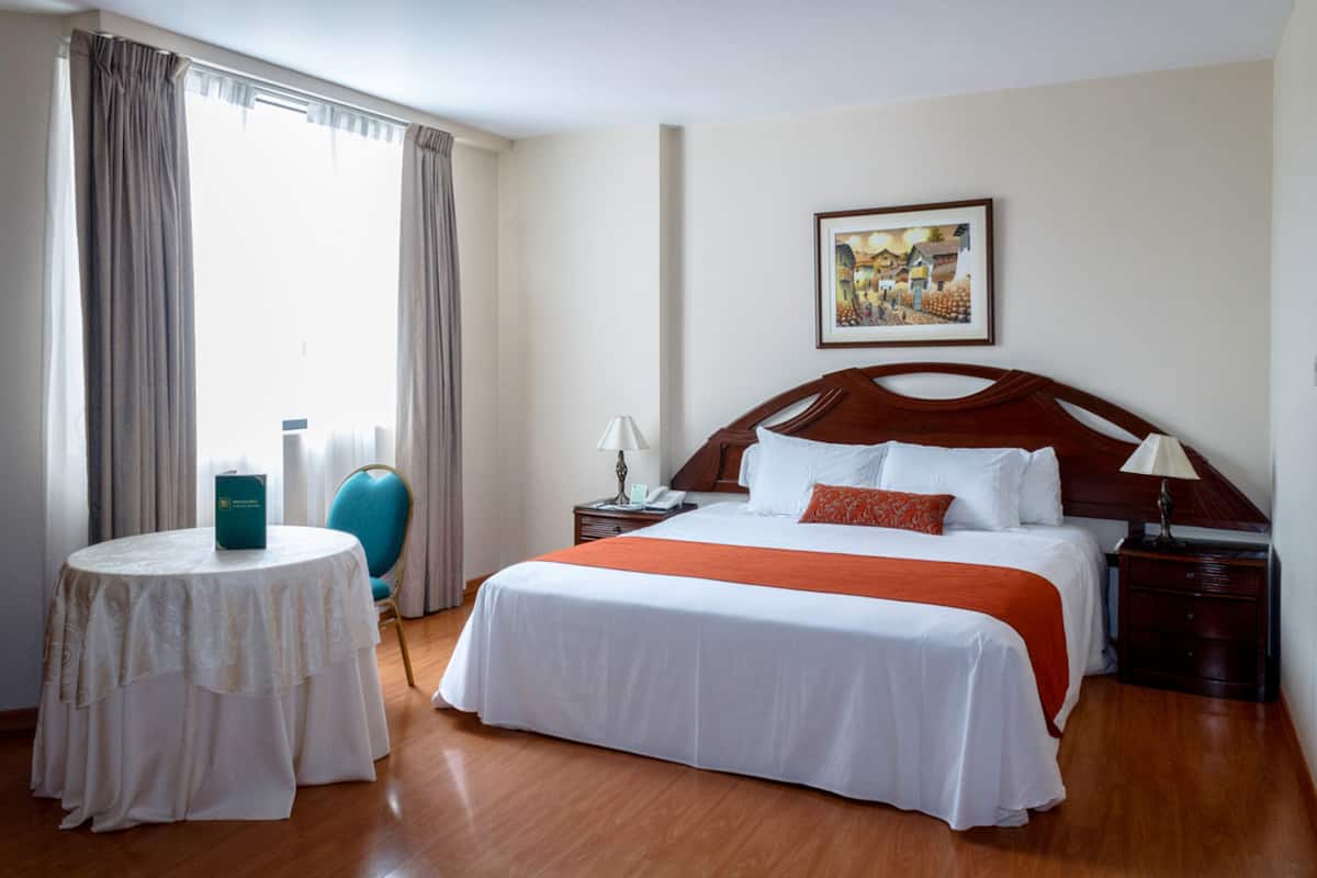 Quarto de hotel com uma cama grande, uma mesa redonda, uma cadeira e um quadro na parede.