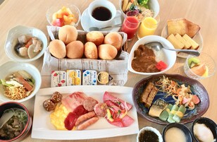 Uma mesa com diversos itens de café da manhã, incluindo pão, ovos, linguiça e acompanhamentos variados.