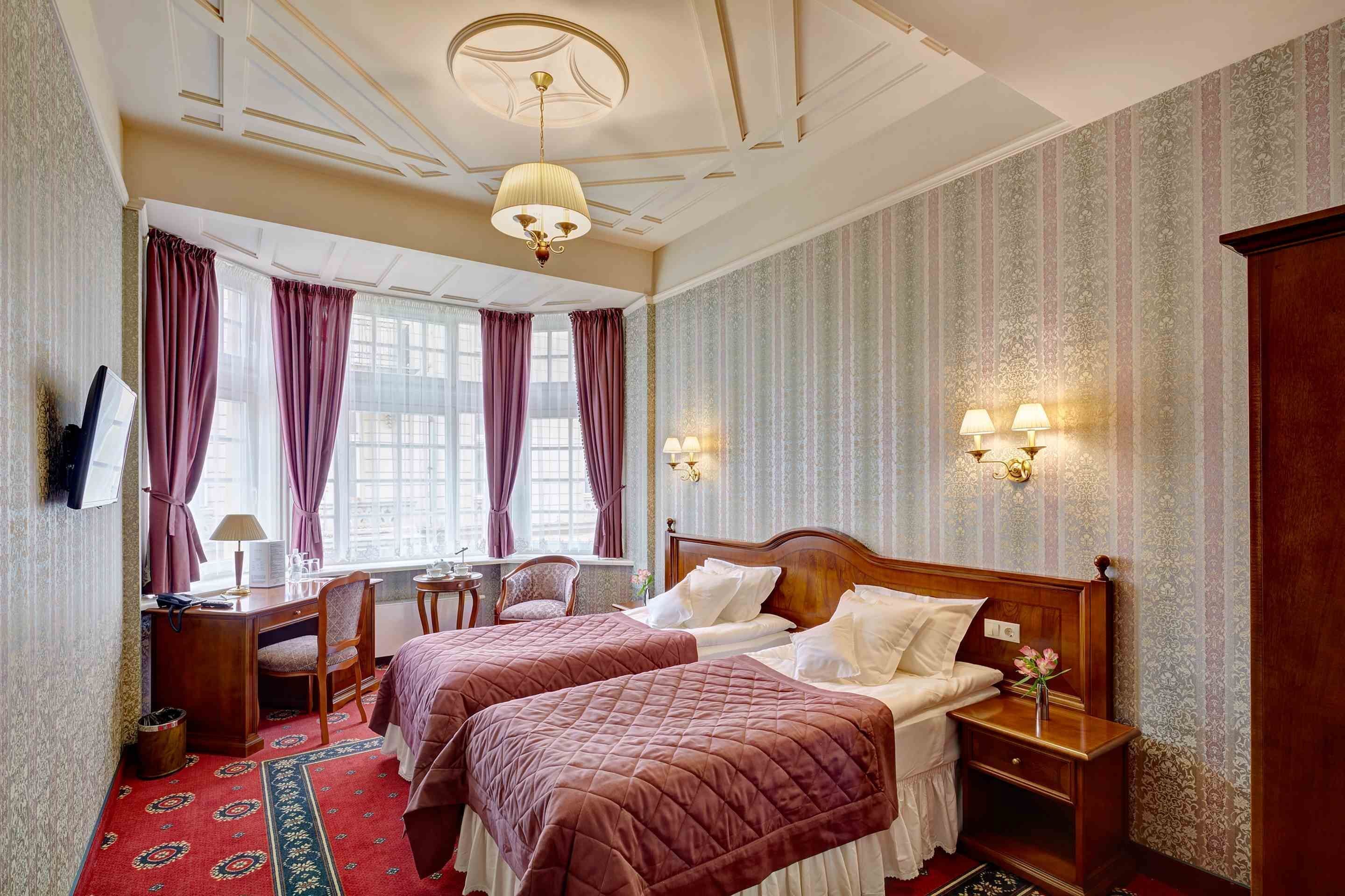 Quarto de hotel com duas camas, uma escrivaninha, uma cadeira, uma televisão e uma janela com cortinas.