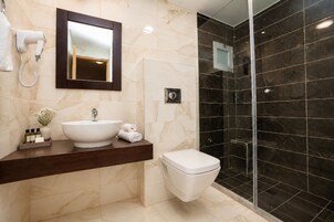 Casa de banho moderna com lavatório branco, sanita, secador de cabelo e cabine de duche em vidro.