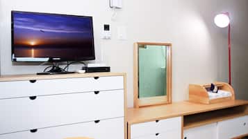 Quarto moderno com televisão sobre uma escrivaninha de madeira, um espelho, luminária de mesa e uma cama de madeira.