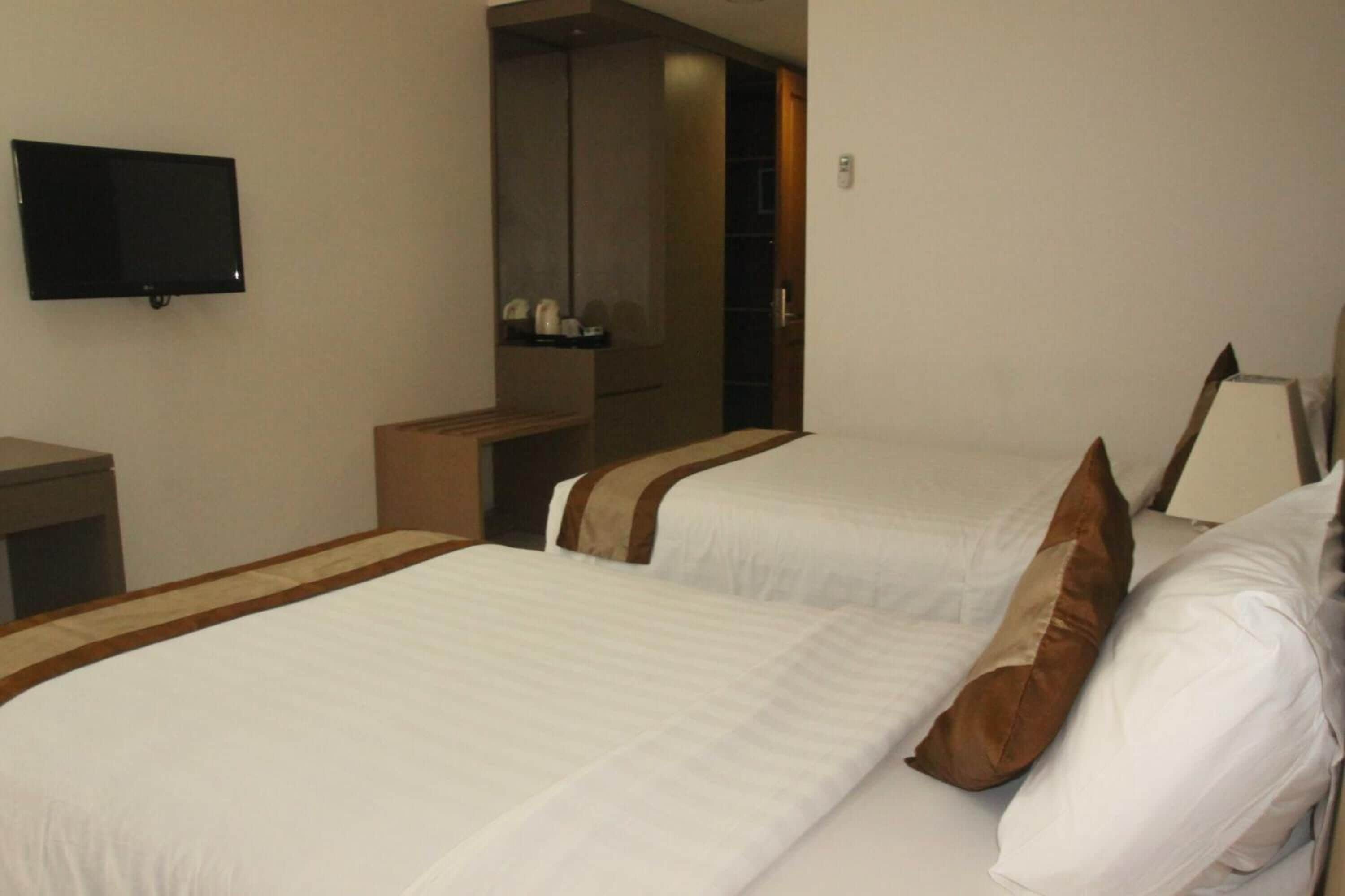 Quarto de hotel com duas camas, uma televisão de tela plana na parede e um espelho sobre as camas.