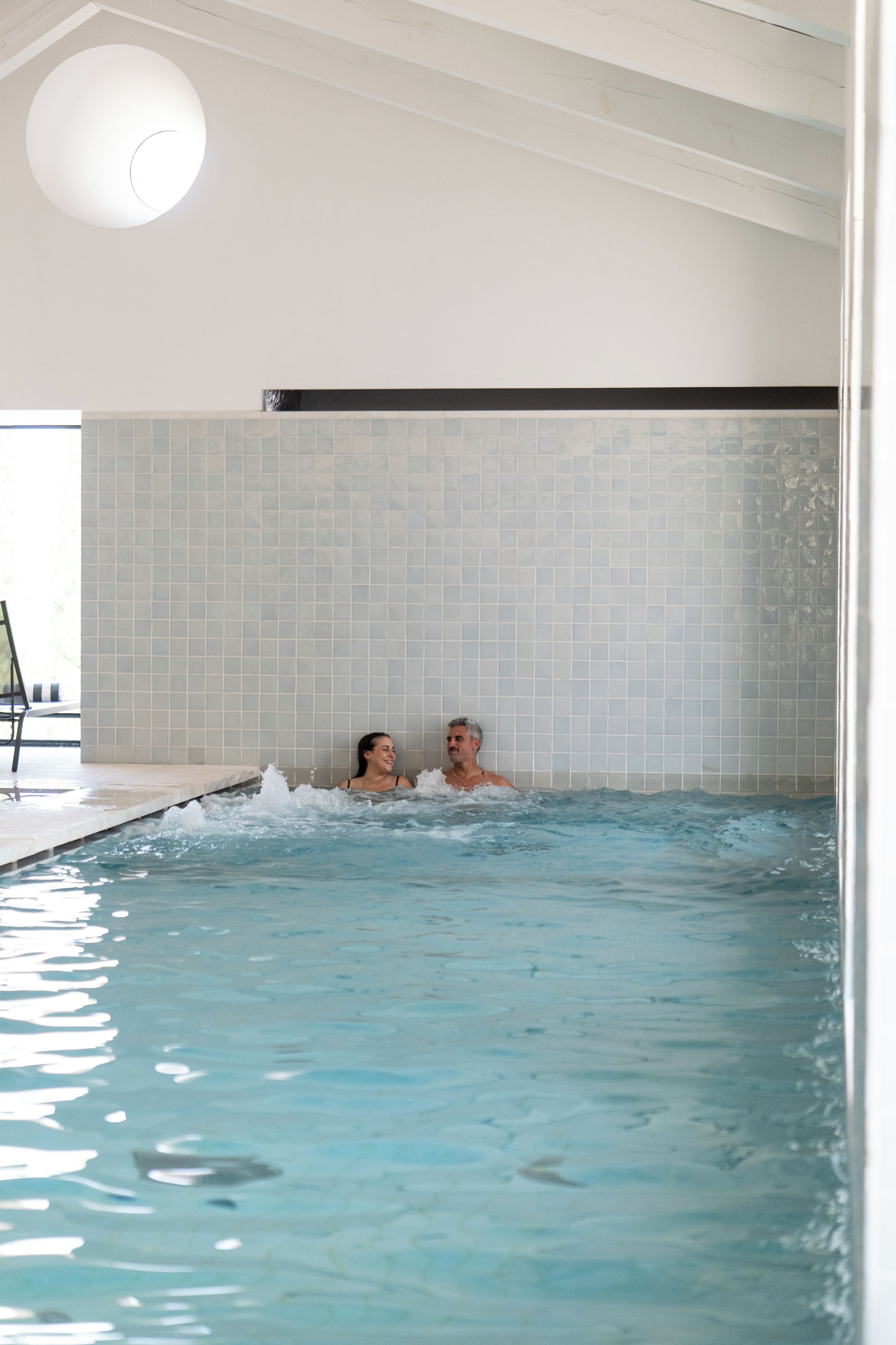 Piscina interna com paredes azulejadas e luminária no teto.