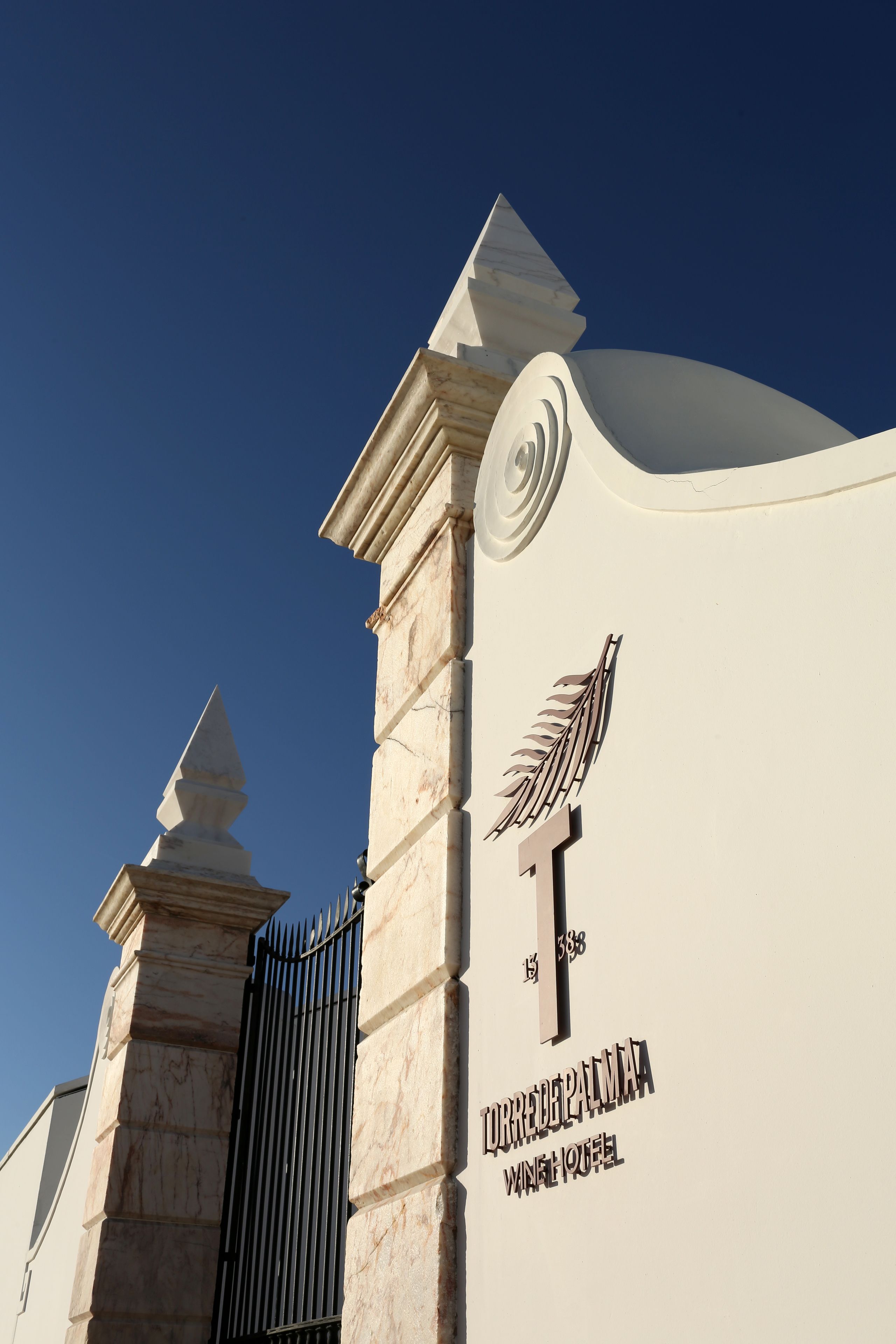 Um edifício com estilo arquitetônico clássico, apresentando uma entrada imponente com portão decorativo e um emblema alado.