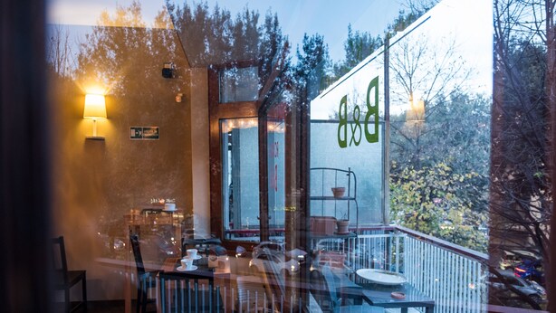 Restaurante com área externa, parede de vidro e vista para árvores.