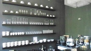 Uma área de bar com prateleiras cheias de copos e copos brancos, uma máquina de café e diversas garrafas.