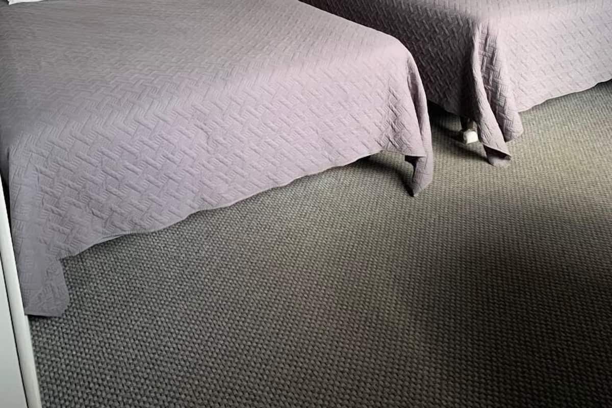 Quarto de hotel com duas camas, uma cabeceira de madeira, uma janela com cortinas e duas luminárias fixadas na parede.