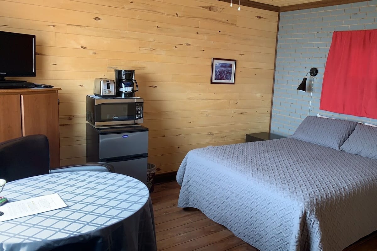 Quarto compacto com uma cama, uma mesa com jogo americano, micro-ondas, cafeteira e televisão sobre um móvel.
