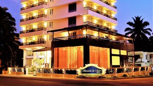 Um hotel de vários andares com varandas, uma placa com a inscrição "Paranda do Mar" e uma palmeira ao fundo.