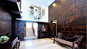 Um hall amplo com piso de mármore, balcão de recepção de madeira, sofá estampado e escada para um andar superior.