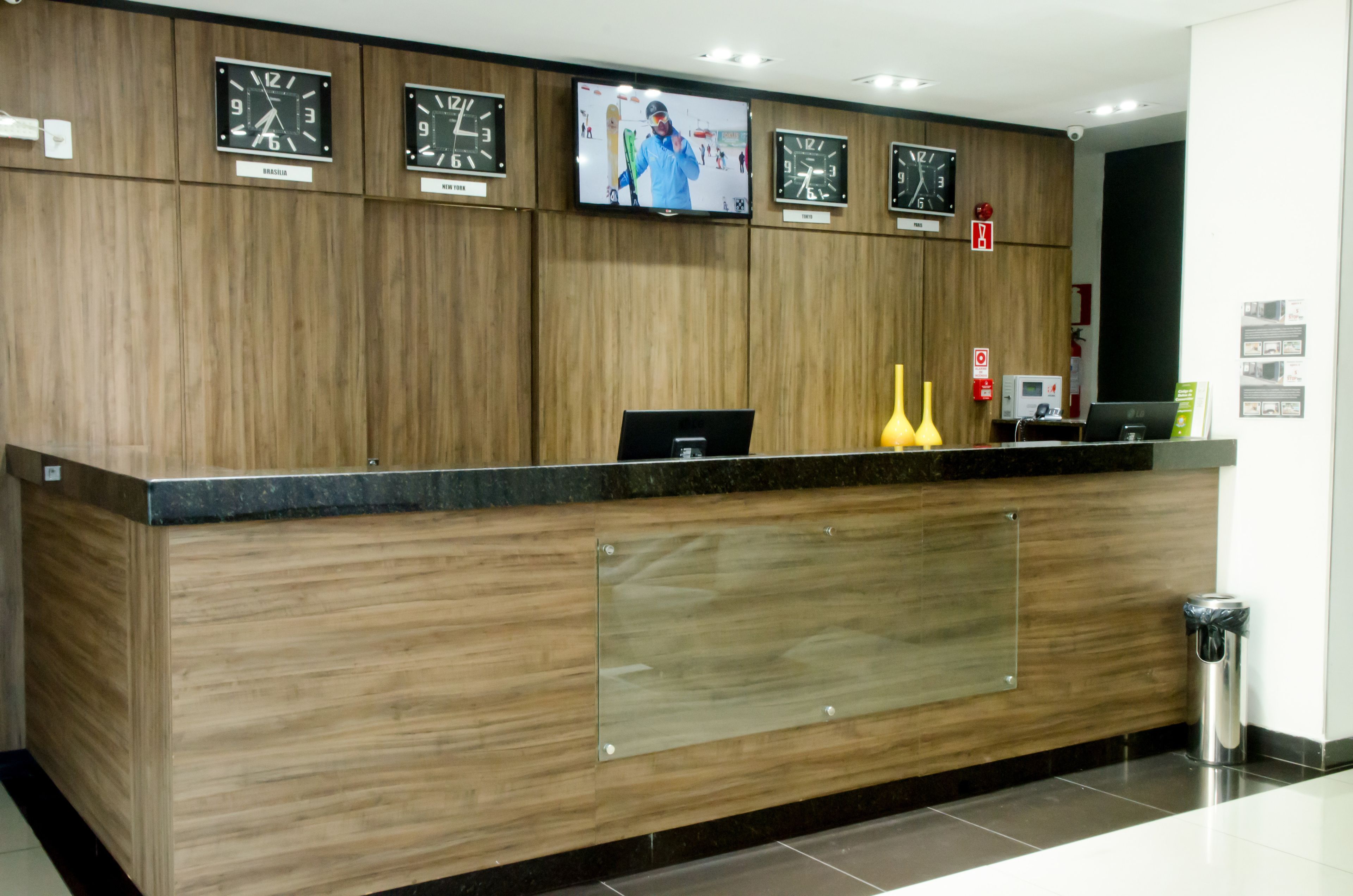Uma mesa de recepção com acabamento em madeira, vários relógios, uma tela de televisão e uma lixeira.
